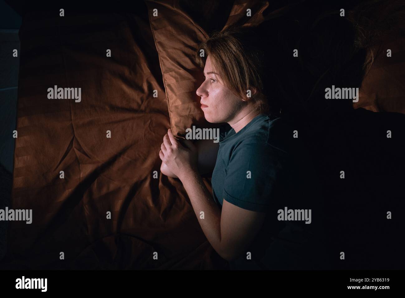 Young sad woman lying in bed late at night trying to sleep suffering ...