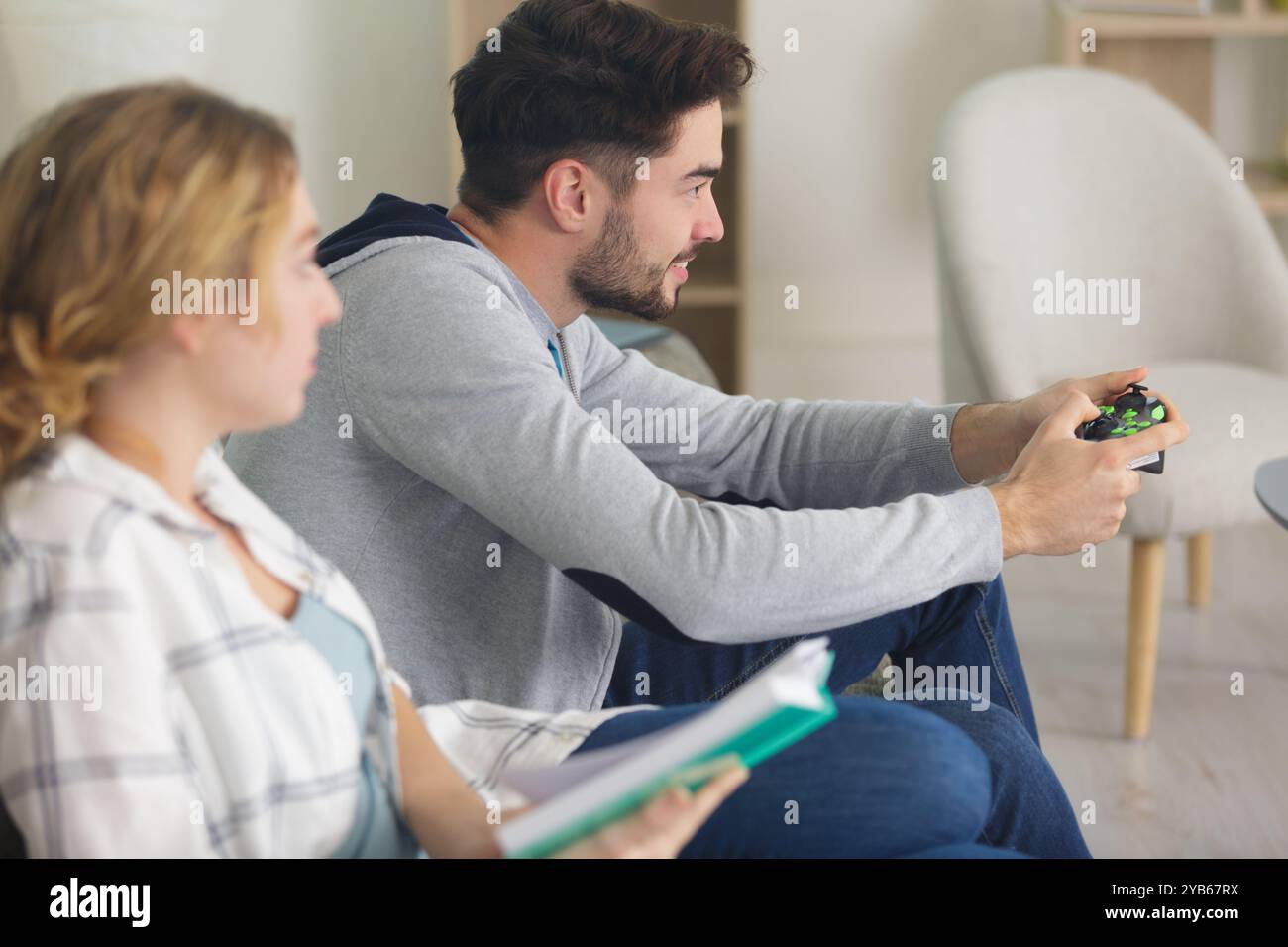 woman reading while her partner plays a computer game Stock Photo - Alamy