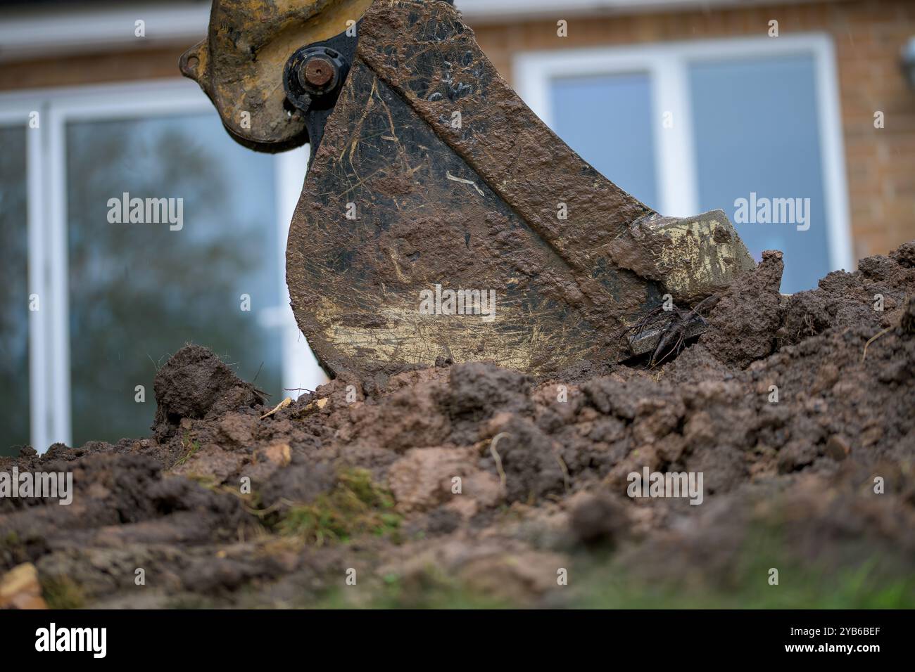A side view of a diggers bucket resting on a mound of mud in front of a ...