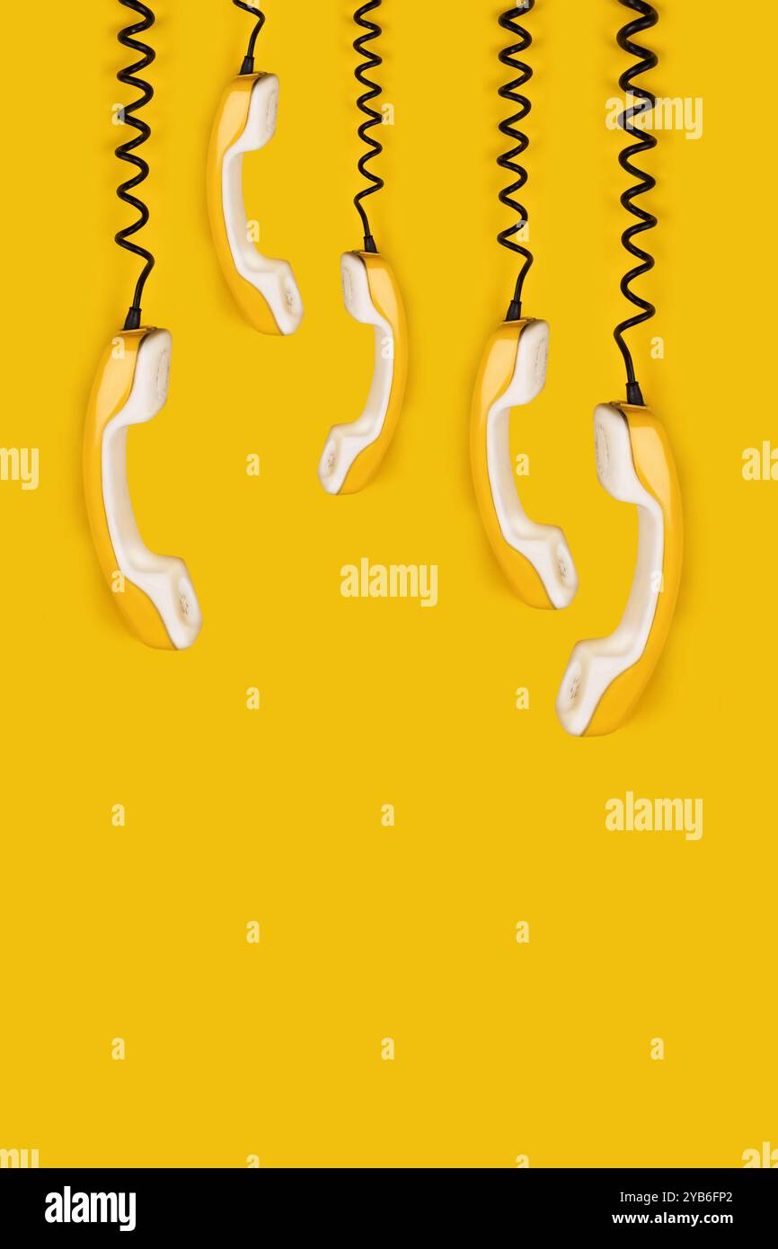 A few yellow old phone handsets dangle on wire. yellow background ...