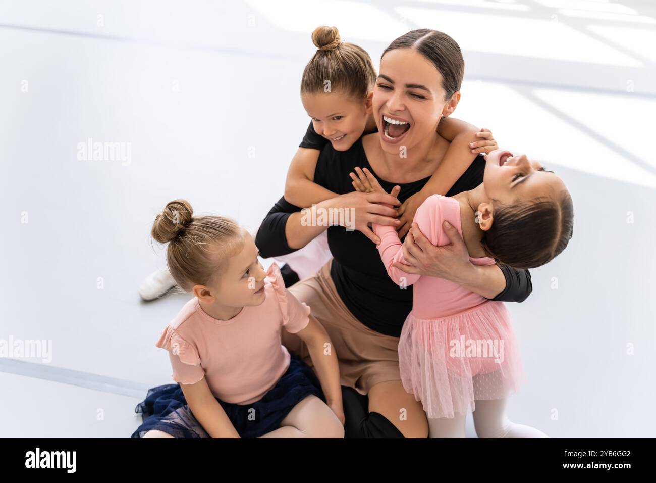 Laughing young ballerina hugging her little pupils in ballet class ...