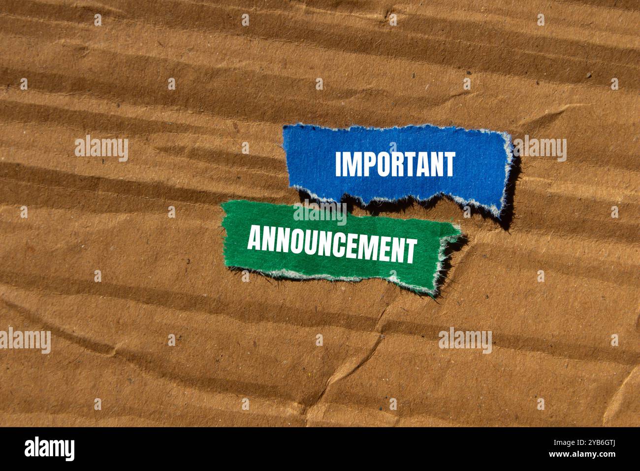 Important announcement message written on ripped torn paper pieces with cardboard background ...