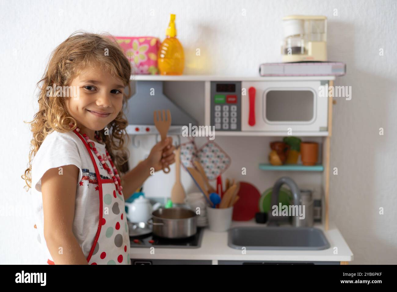 A cheerful young girl smiles while holding a cooking utensil, playing ...