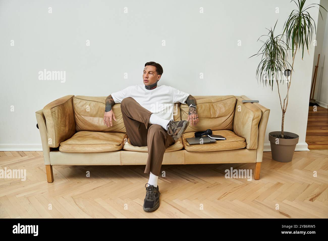 A young handsome man lounges comfortably on a modern sofa, reflecting ...