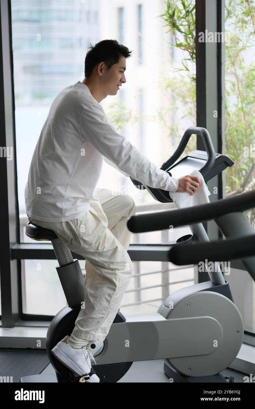side view of handsome Asian young man ride on exercise bike in gym ...