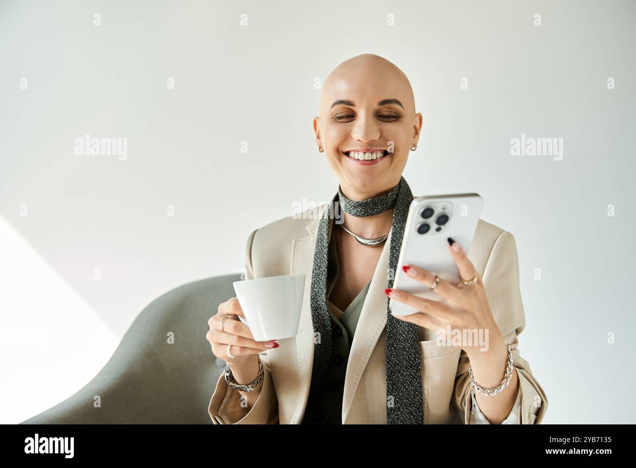 A joyful bald woman sips tea and engages with her phone, radiating ...