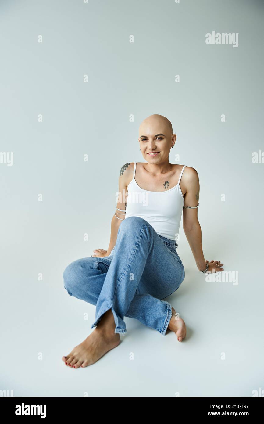 A young bald woman with alopecia sits casually on a smooth surface ...