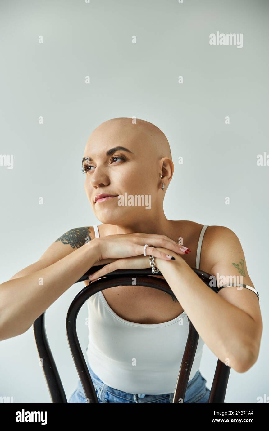 A young bald woman smiles softly while resting her arms on a chair ...