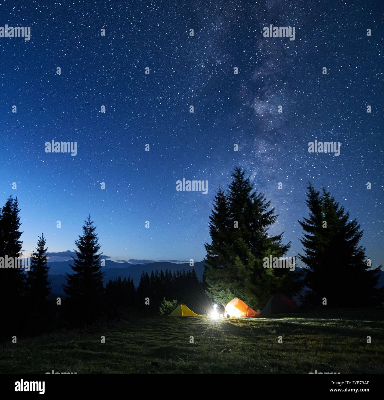 Night camping in mountains. Amidst forested mountain landscape, two ...
