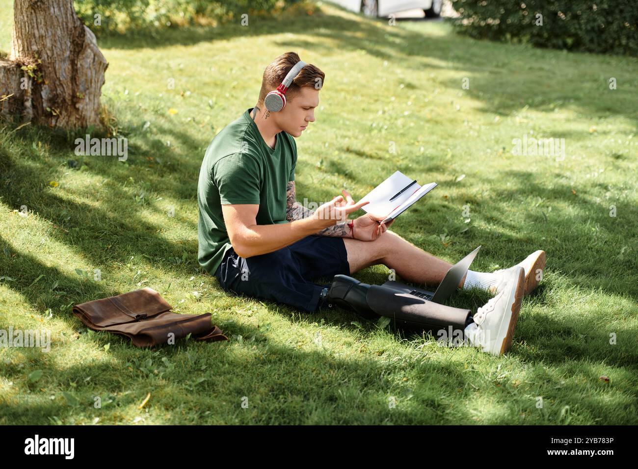 A young man relaxes on the grass, reading a book while sporting a ...