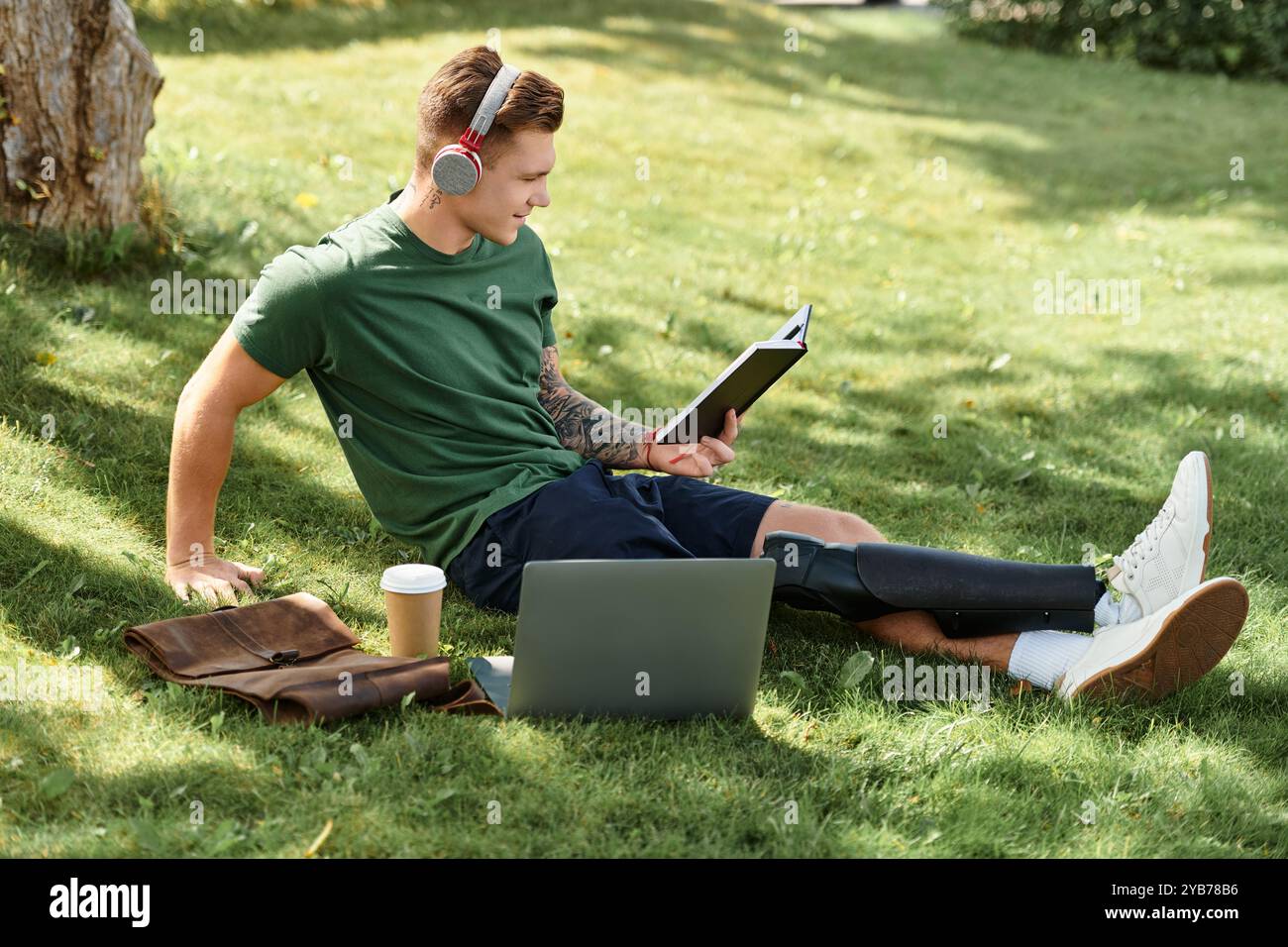 A young man with a prosthetic leg smiles while reading a book on lush ...