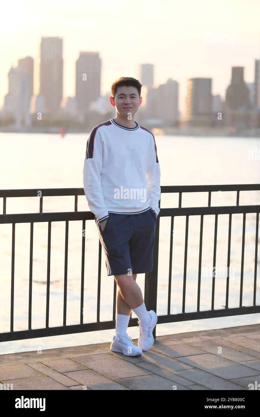 smiling Asian young man standing at dusk outdoor, looking at camera ...