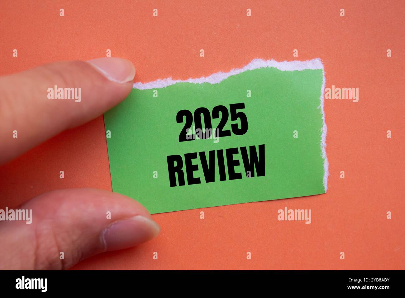 2025 review message written on ripped torn green paper piece with orange background. Conceptual ...