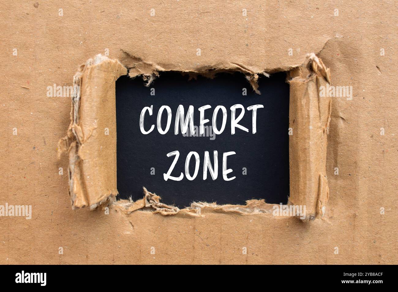 Comfort zone message written on ripped torn cardboard paper with black background. Conceptual ...