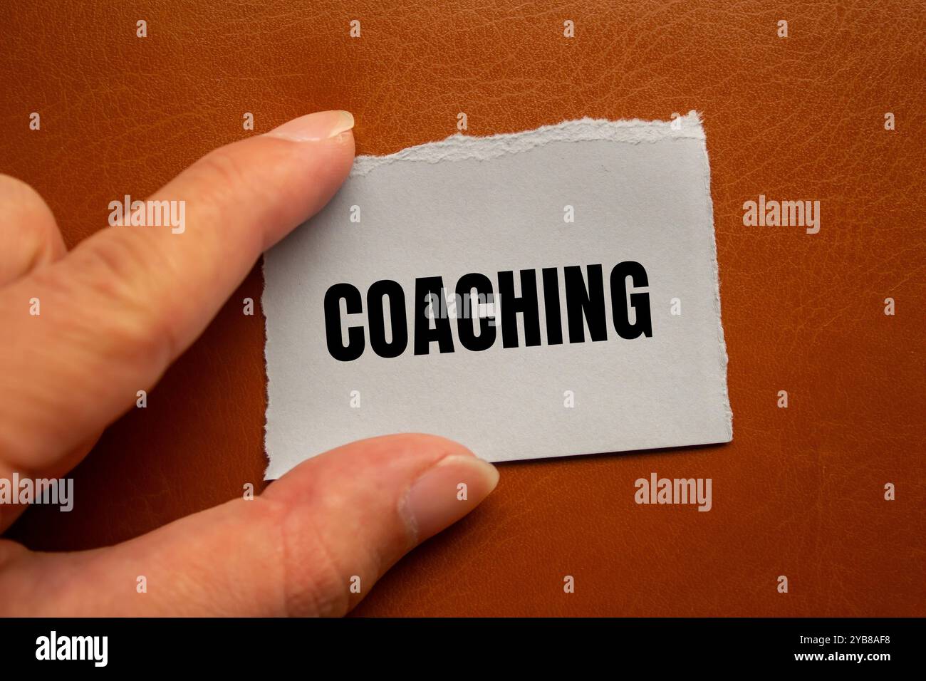 Coaching message written on ripped torn paper piece with brown background. Conceptual coaching ...