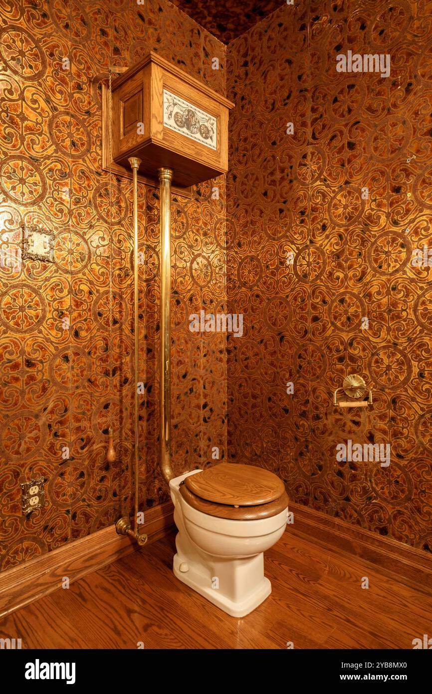 A high tank pull chain toilet with copper coloured wallpaper and wooden ...