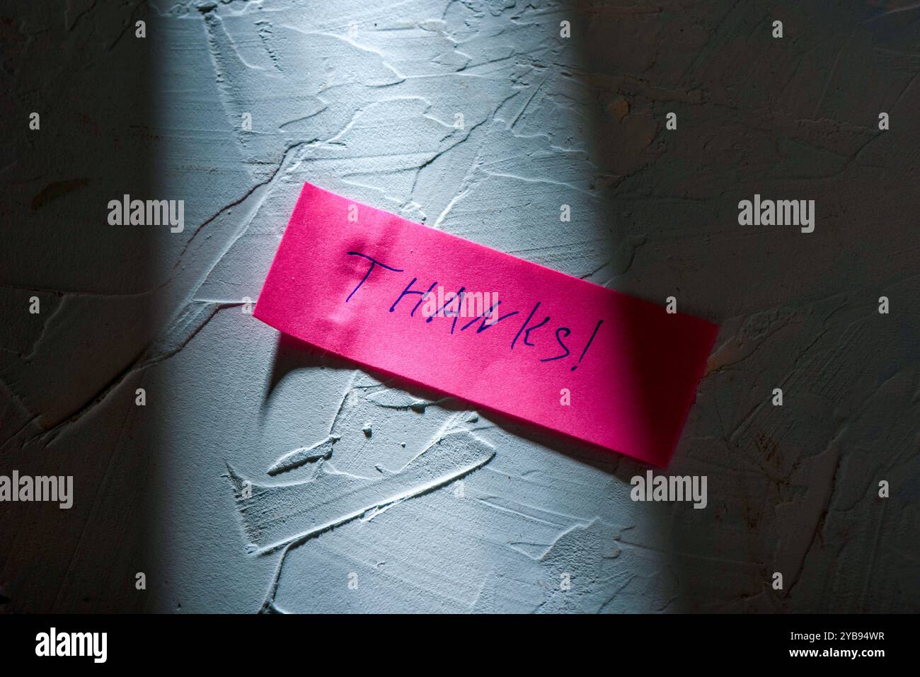 A vibrant pink sticky note saying Thanks placed on a textured wall ...
