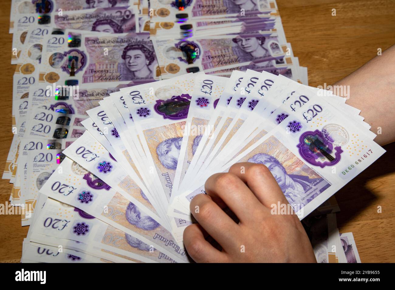 A close-up of a hand holding a fan of twenty-pound banknotes, with a ...
