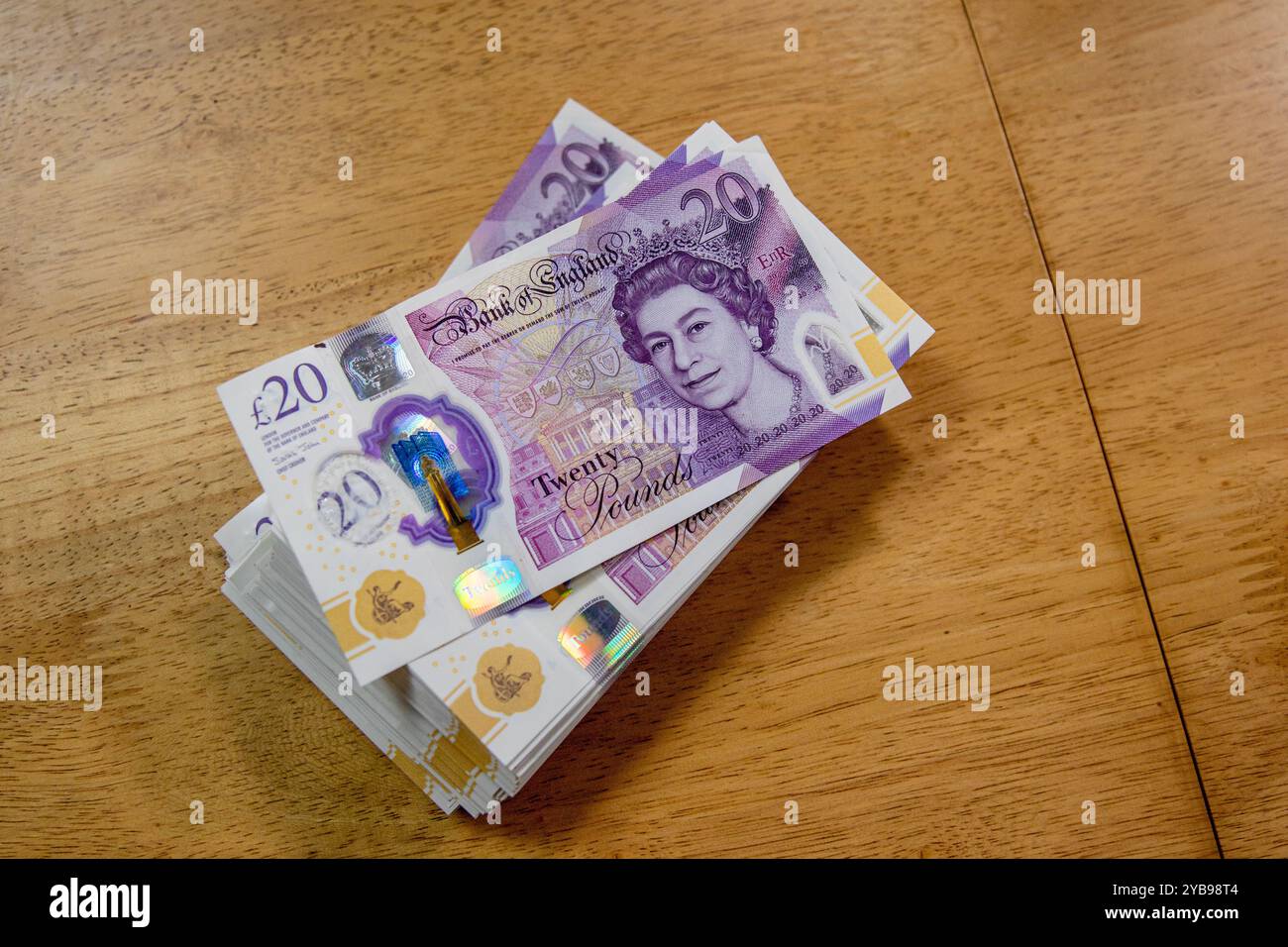 A stack of twenty-pound banknotes arranged neatly on a wooden table ...