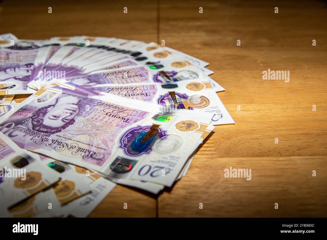 A fan of twenty-pound banknotes arranged on a wooden table. The notes ...