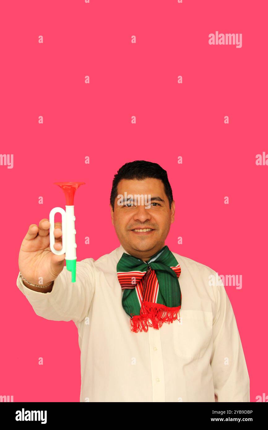 Dark-skinned Mexican adult man with tricolor bow plays a toy trumpet ...