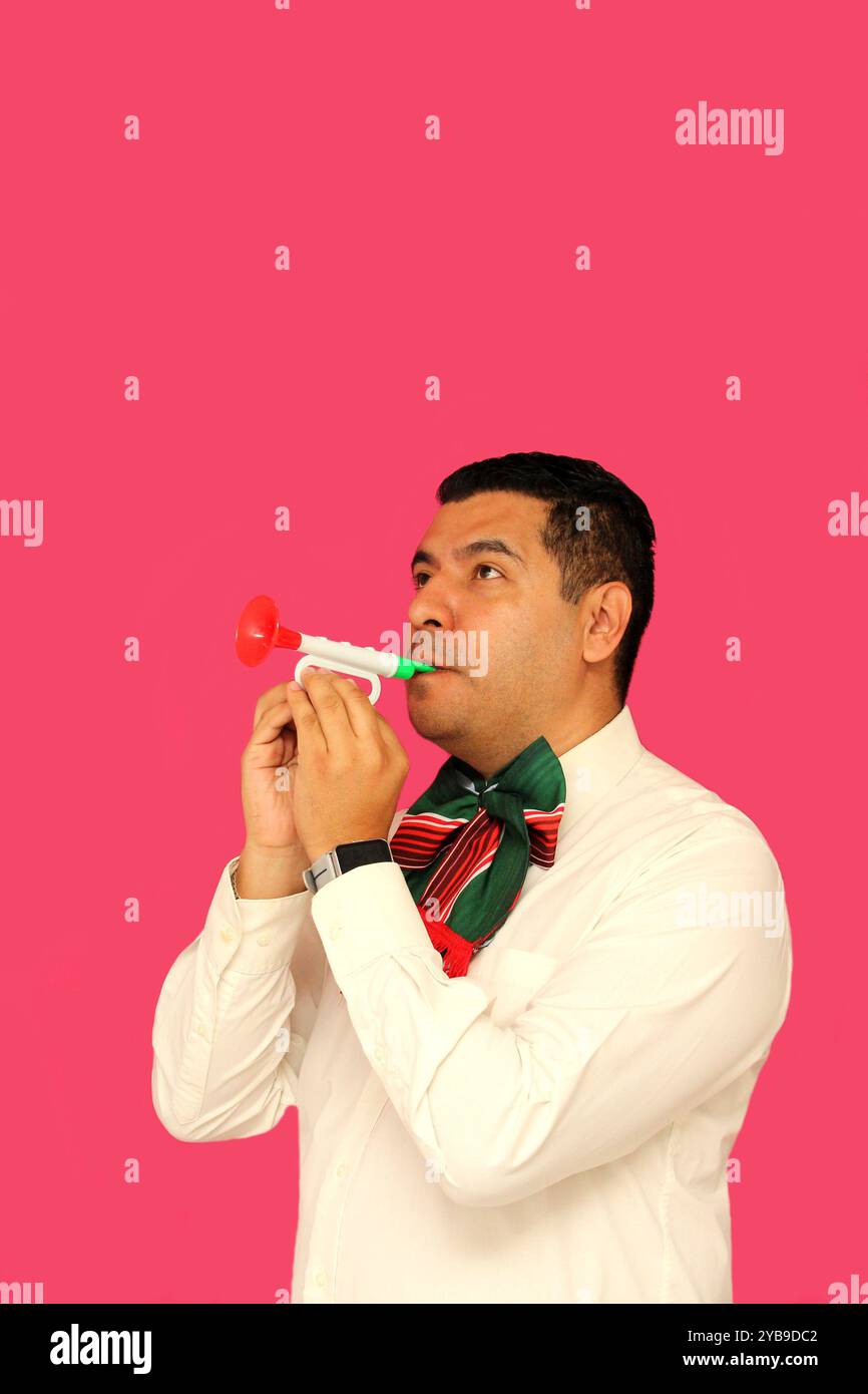 Dark-skinned Mexican adult man with tricolor bow plays a toy trumpet ...