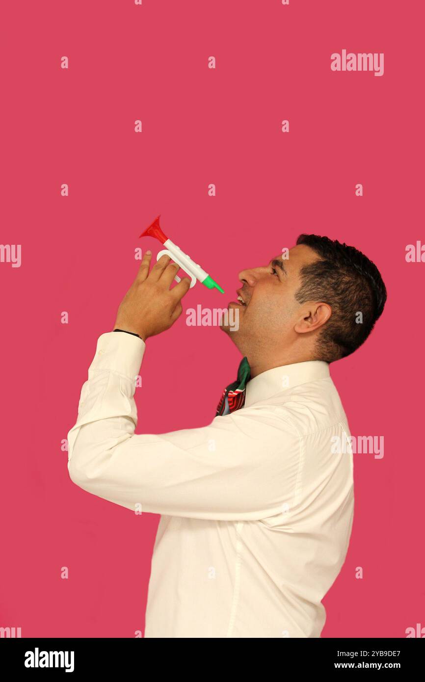 Dark-skinned Mexican adult man with tricolor bow plays a toy trumpet ...