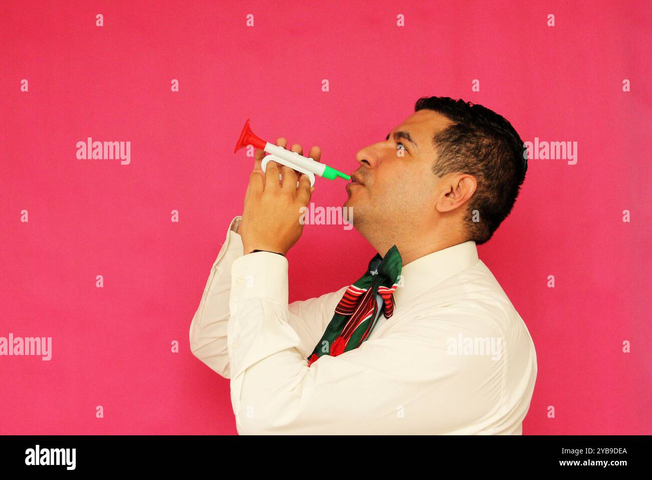 Dark-skinned Mexican adult man with tricolor bow plays a toy trumpet ...