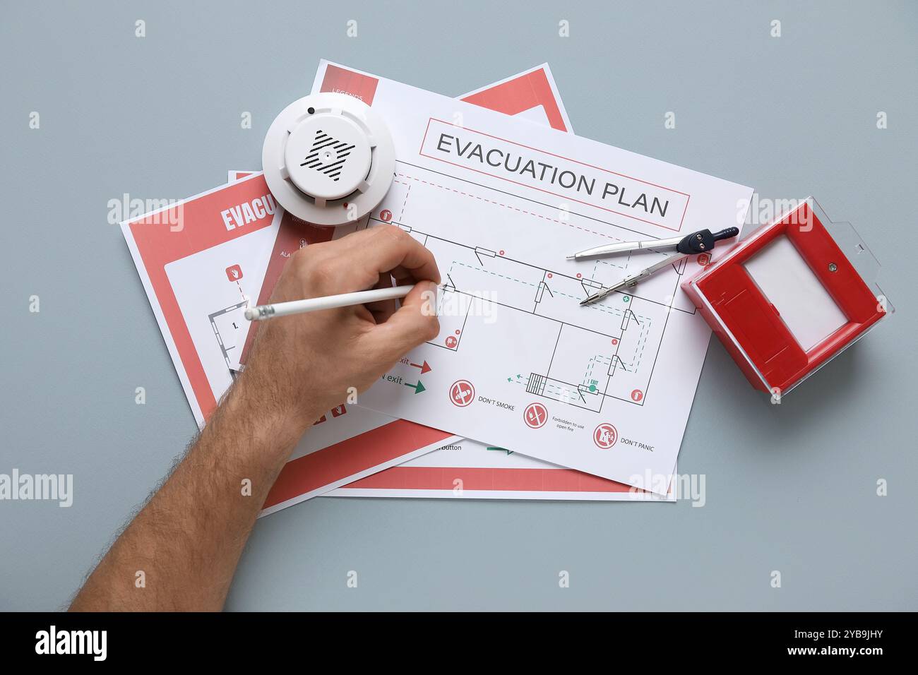 Man with smoke detector drawing evacuation plan on grey background ...