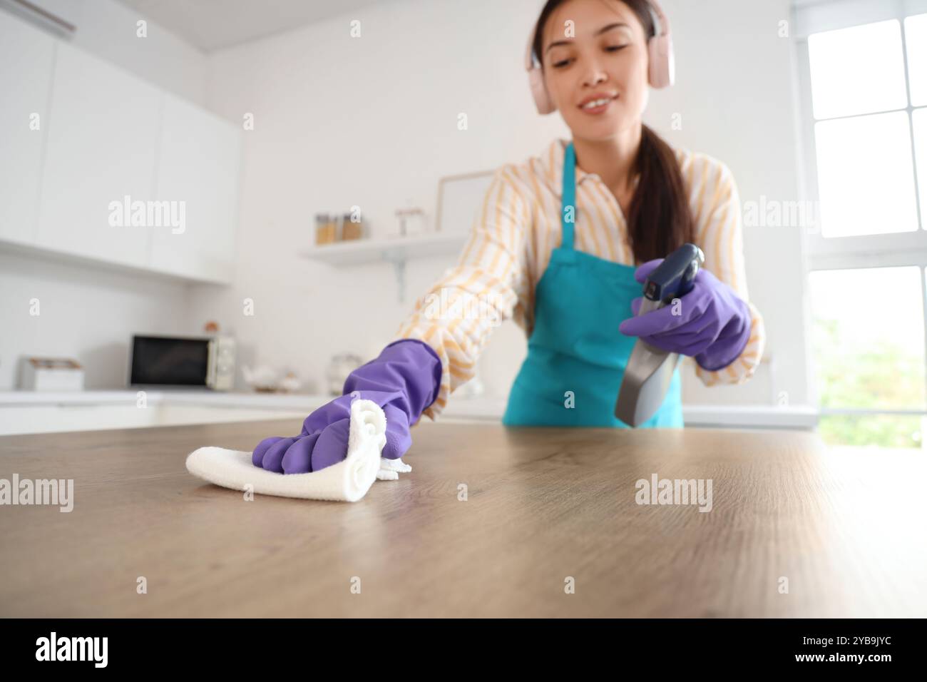 Female Asian janitor with headphones cleaning table in kitchen, closeup ...
