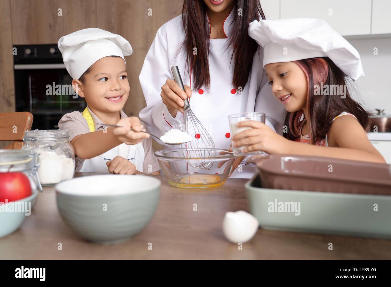 Female Asian chef with her little children making dough at table in ...