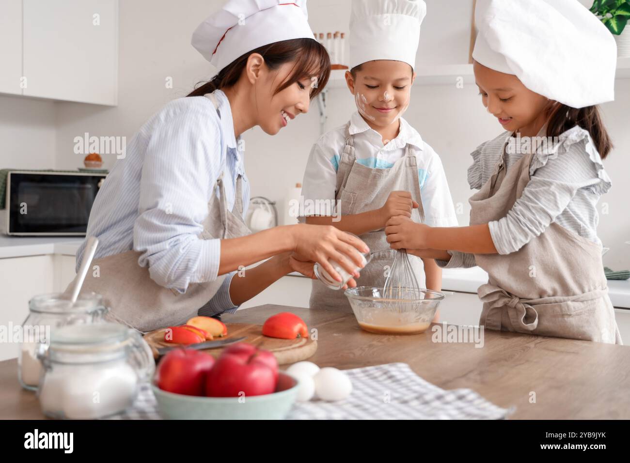 Female Asian chef with her little children making dough in kitchen ...