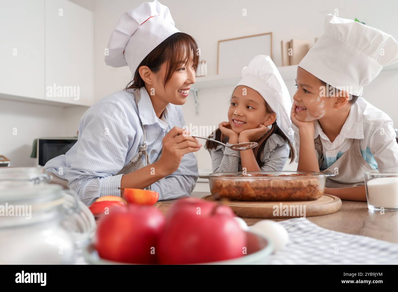 Female Asian chef with her little children cooking apple pie in kitchen ...