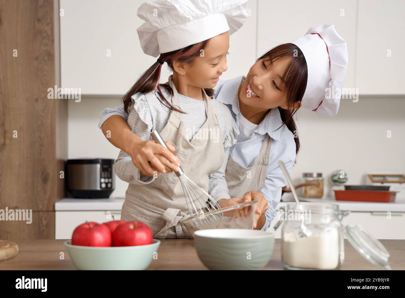 Female Asian chef with her little daughter making dough in kitchen ...