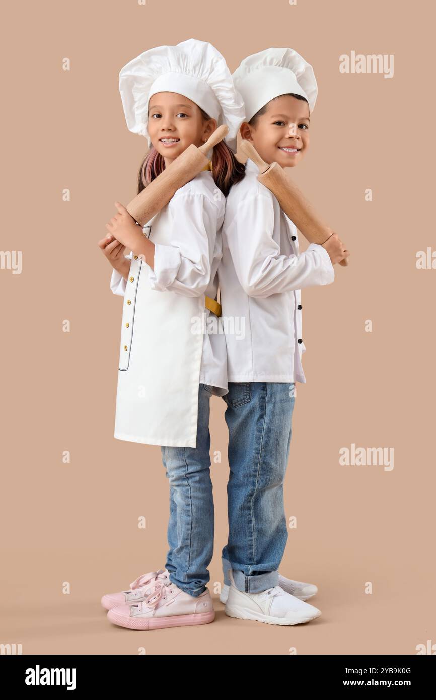 Cute little Asian chefs with rolling pins on beige background Stock ...