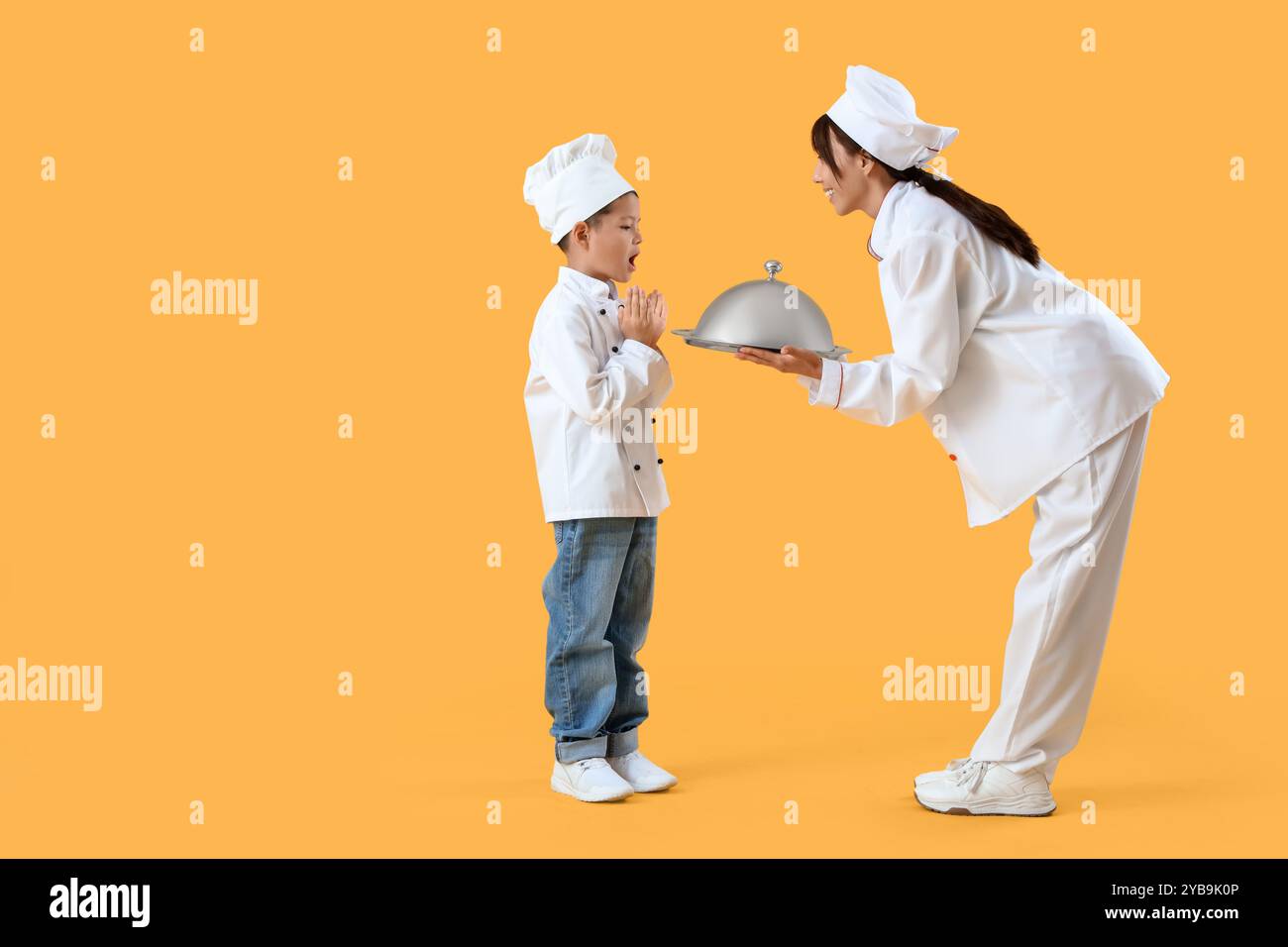 Female Asian chef with cloche and her little son on yellow background ...