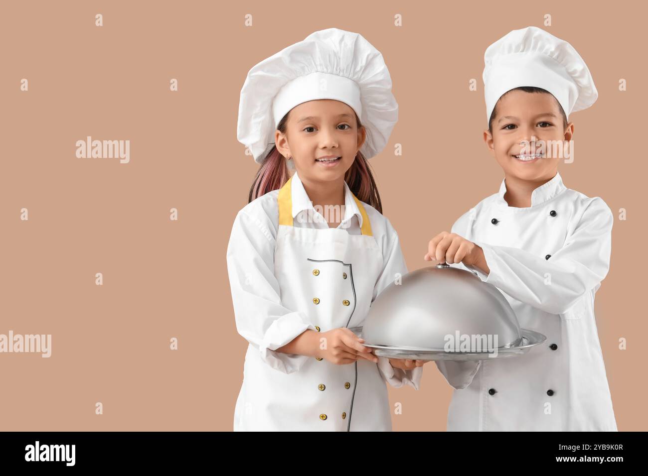 Cute little Asian chefs with cloche on beige background Stock Photo - Alamy