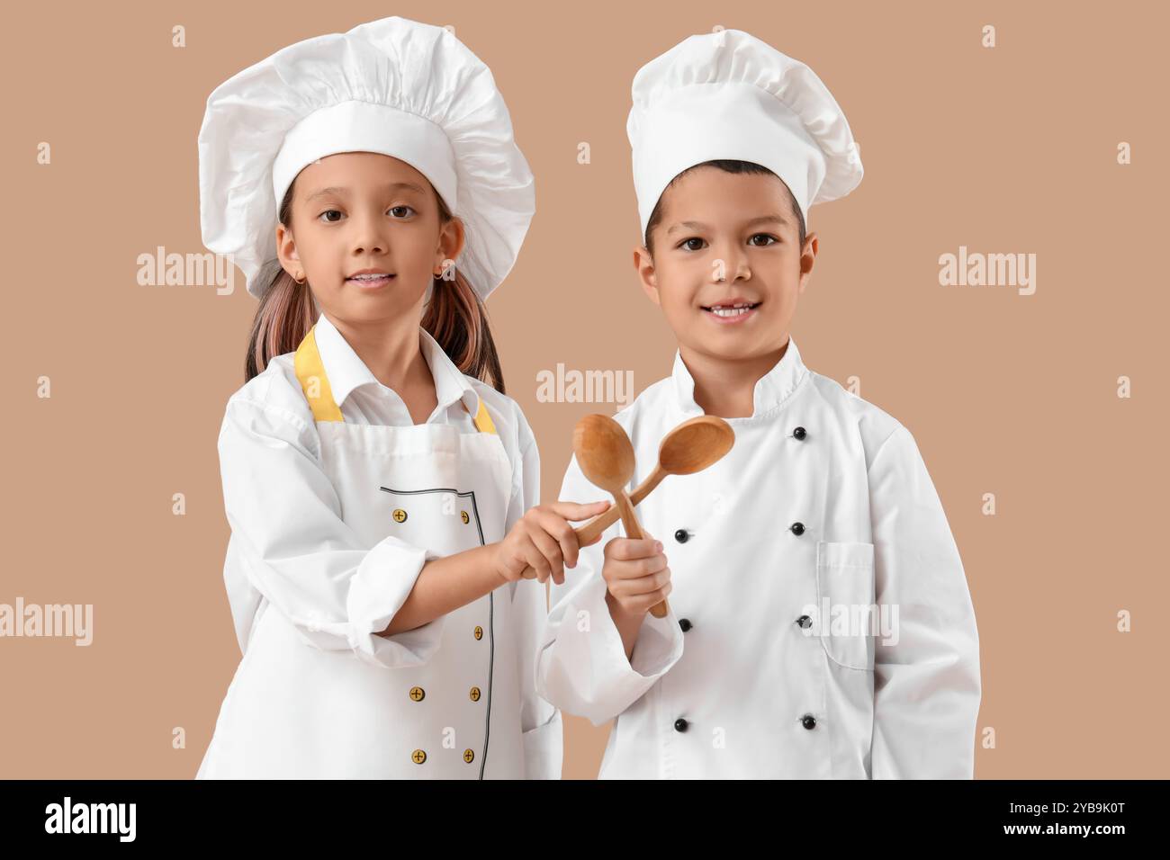 Cute little Asian chefs with wooden spoons on beige background Stock ...