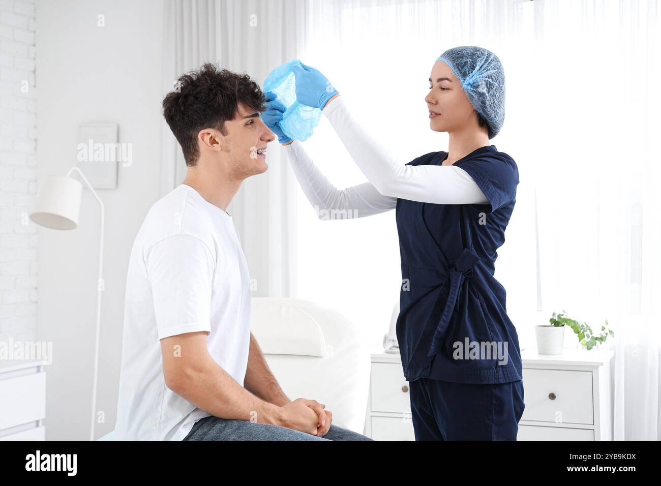 Female plastic surgeon putting hat on young man in clinic Stock Photo ...