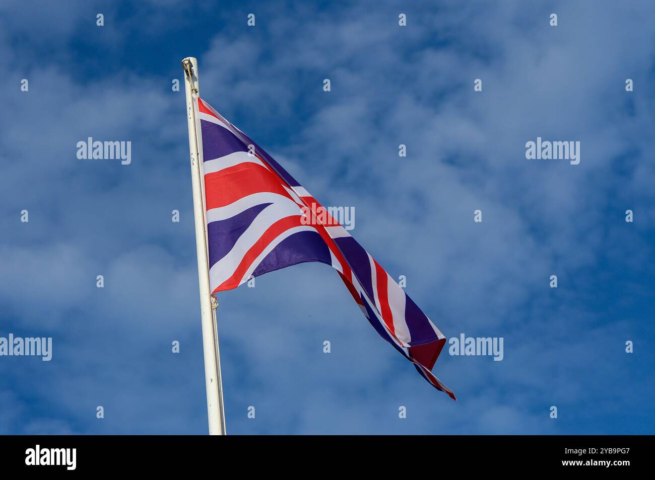 The Union Jack flag flutters gently against a backdrop of fluffy white ...