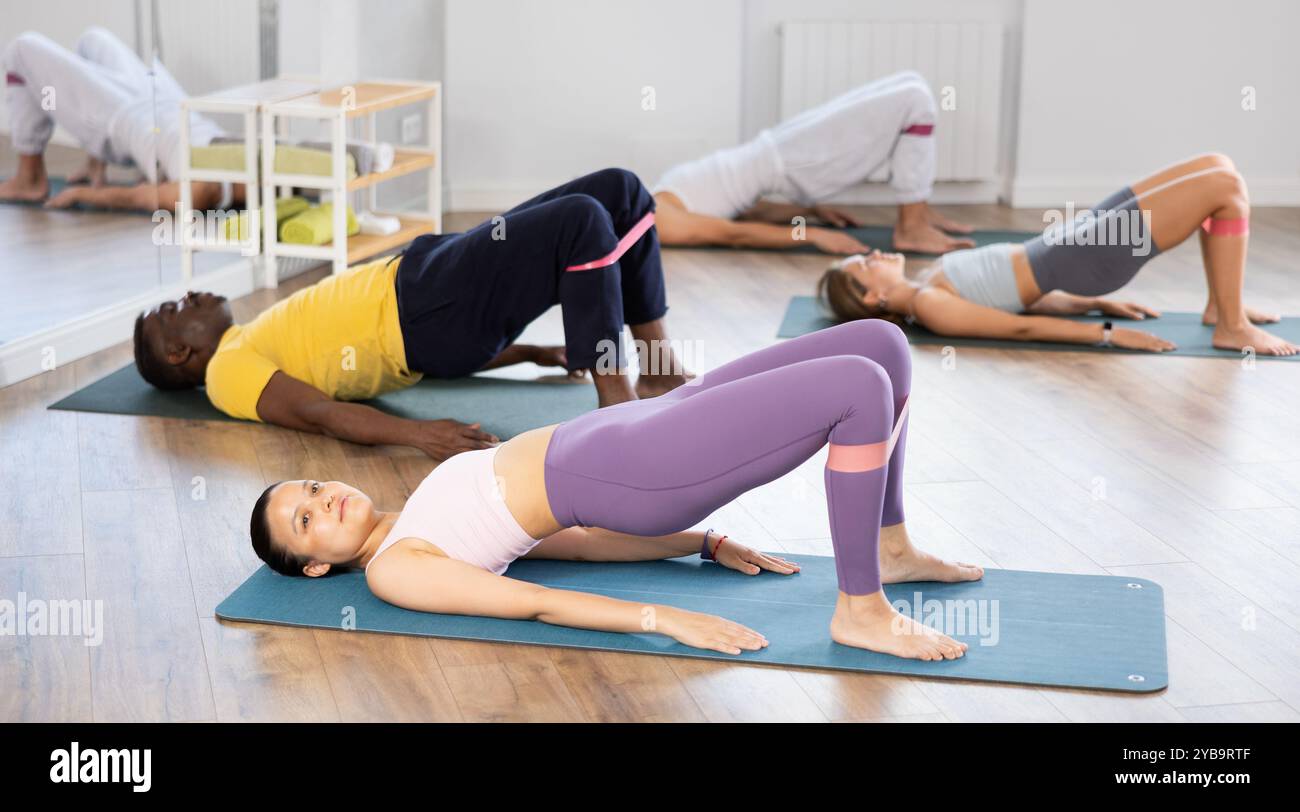 Asian woman performs glute bridge during Pilates multinational training ...