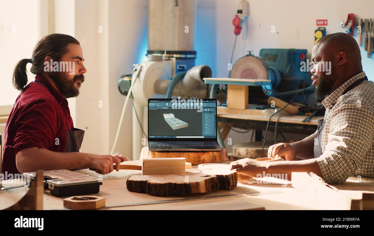 Artisan and apprentice comparing wood art piece with schematic displayed on CAD software on ...