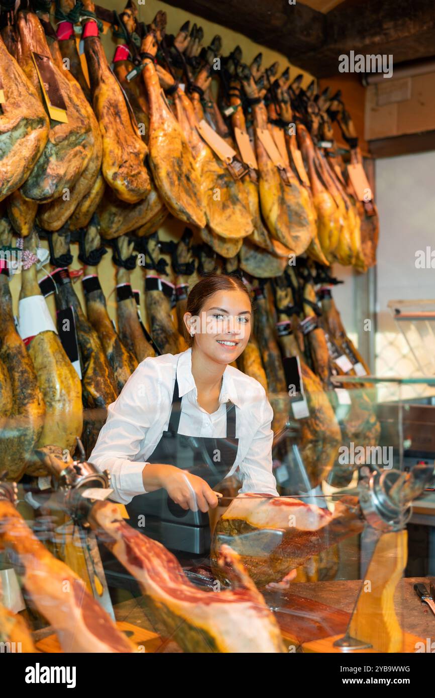 Positive young woman carving jamon slices from pig's leg Stock Photo ...