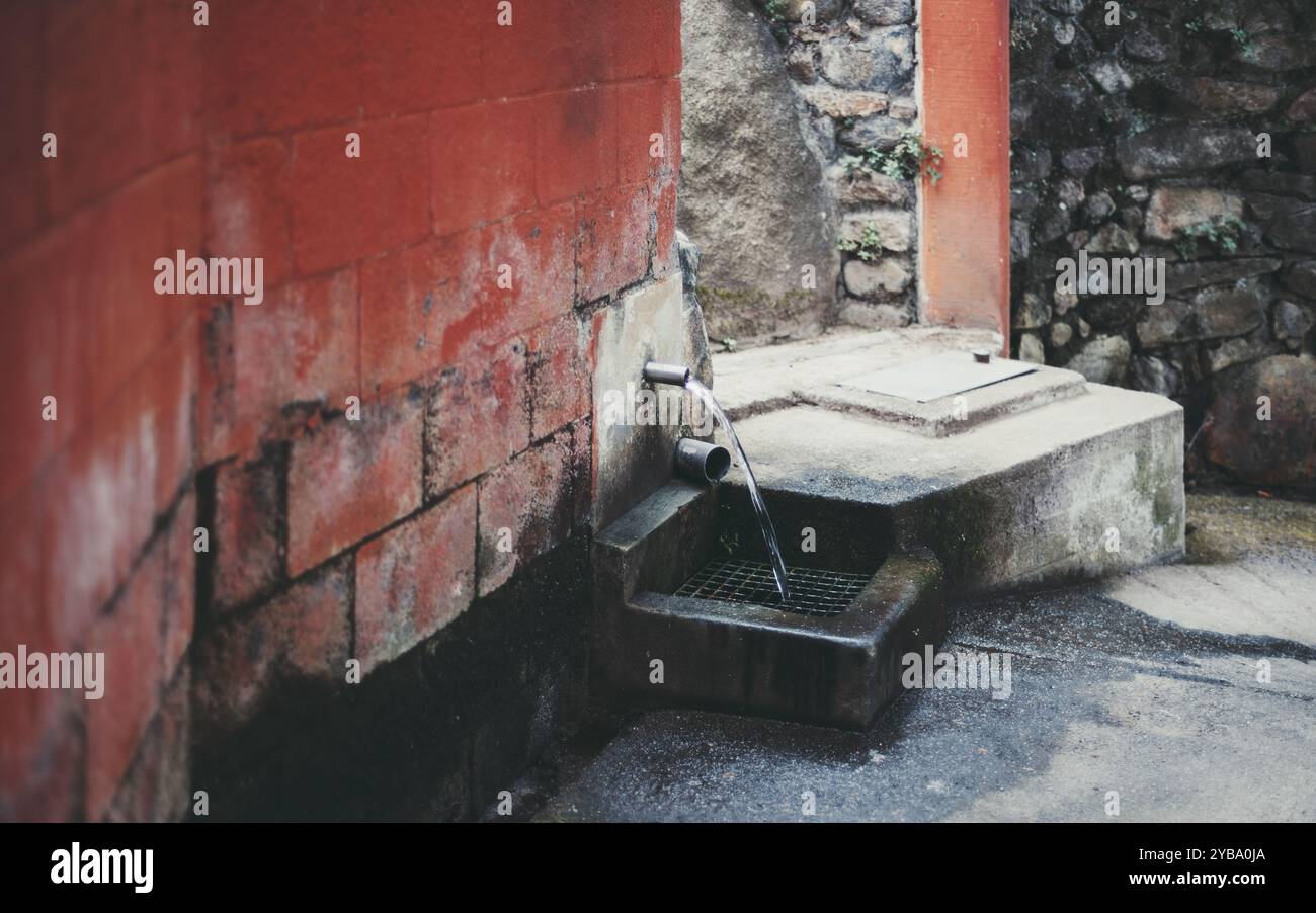 Outdoor water fountain built into a red, weathered wall with mossy ...