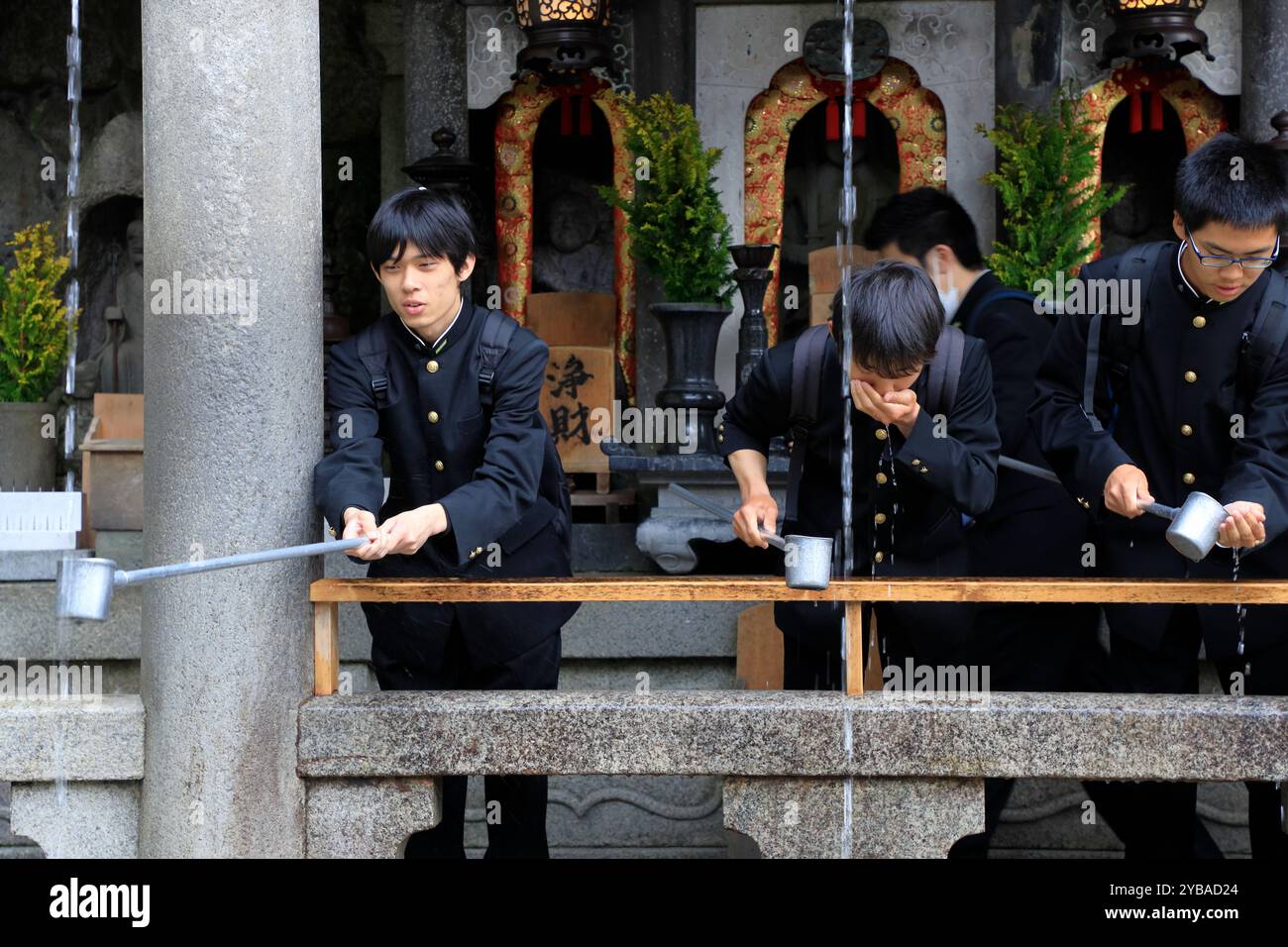 A group of male students in school uniform using cups with long handle ...
