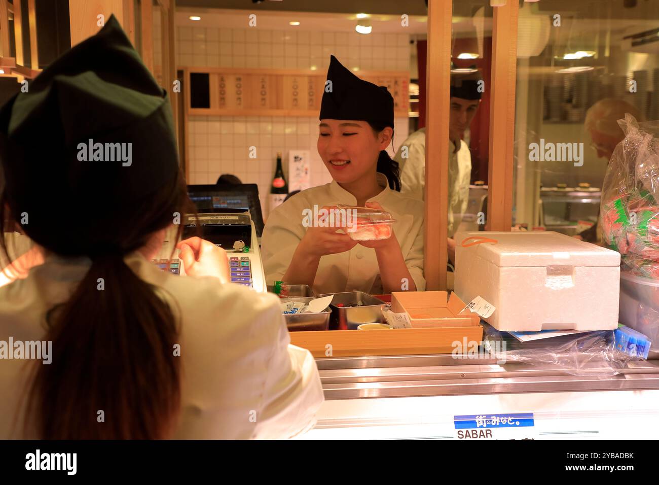 Smiling female employee in uniform working in the ordering window of a ...