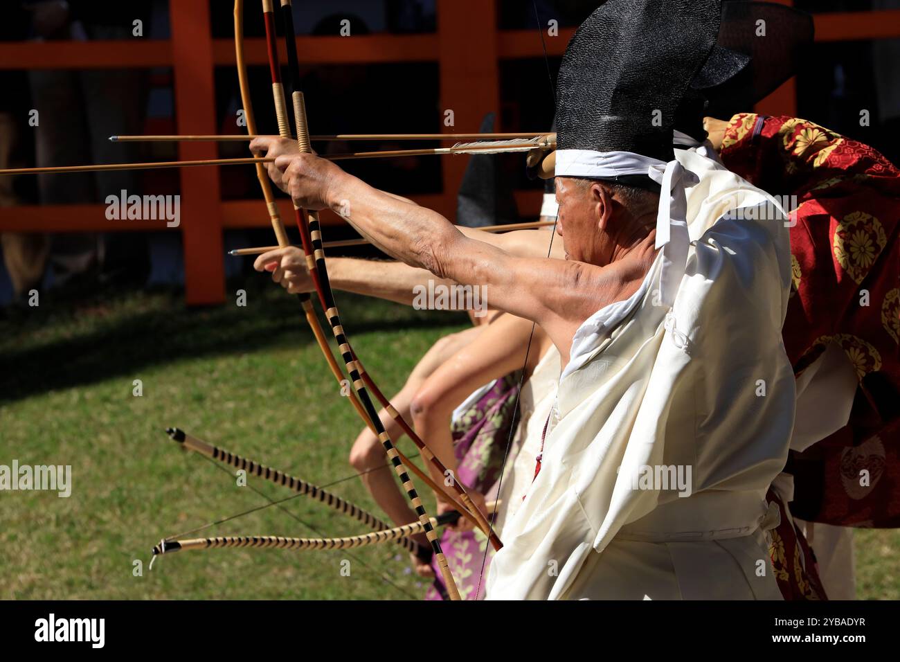 Male archers in traditional ceremonial robe and head piece aiming at ...