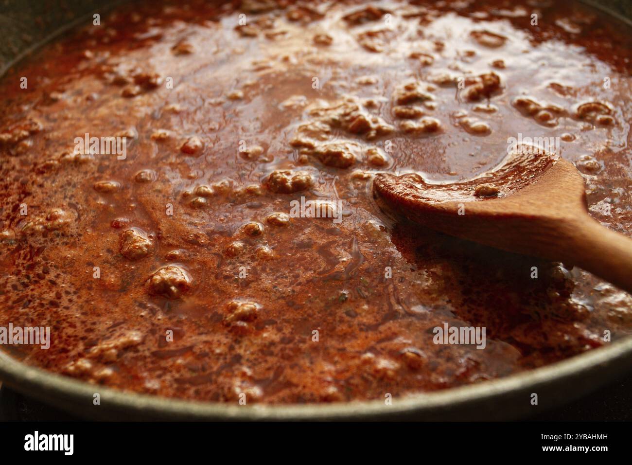 Cooking, bolognese sauce, in a frying pan, stirring with a wooden spoon ...