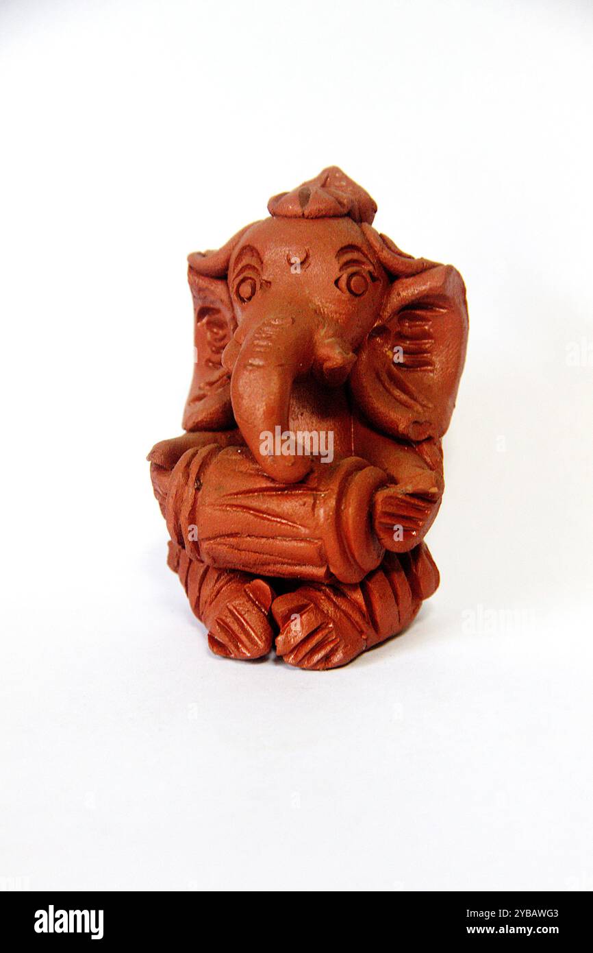View of red mud idol of Ganesha beating drum against white background ...