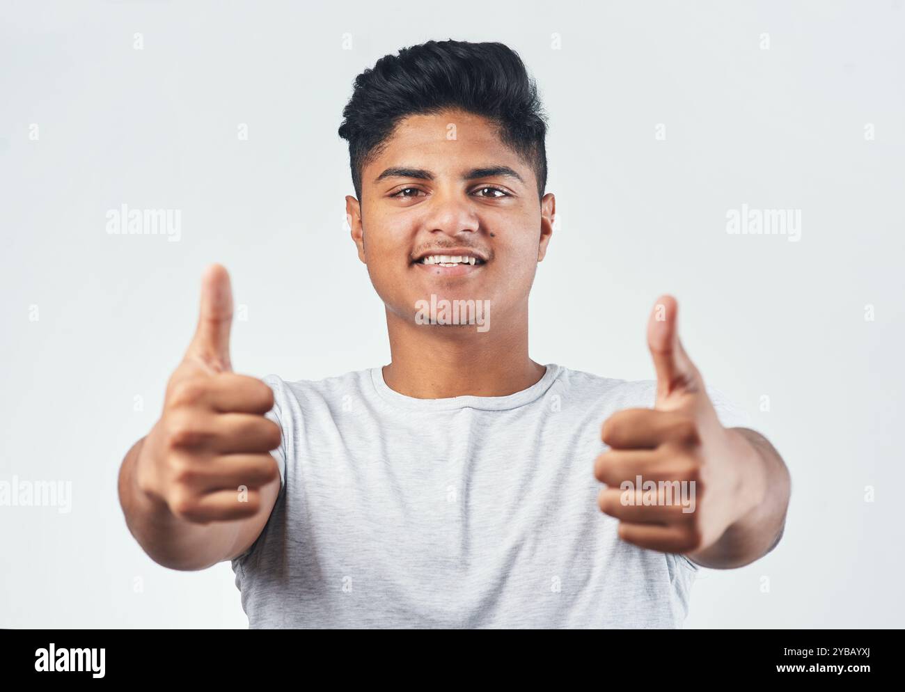 Indian, portrait and happy man with thumbs up for winning, good job or well done on a white ...